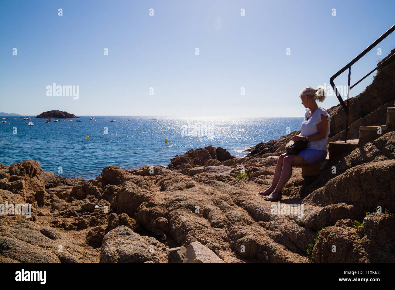 A woman wearing a pale blue top and blue shorts looks out over the bay ...