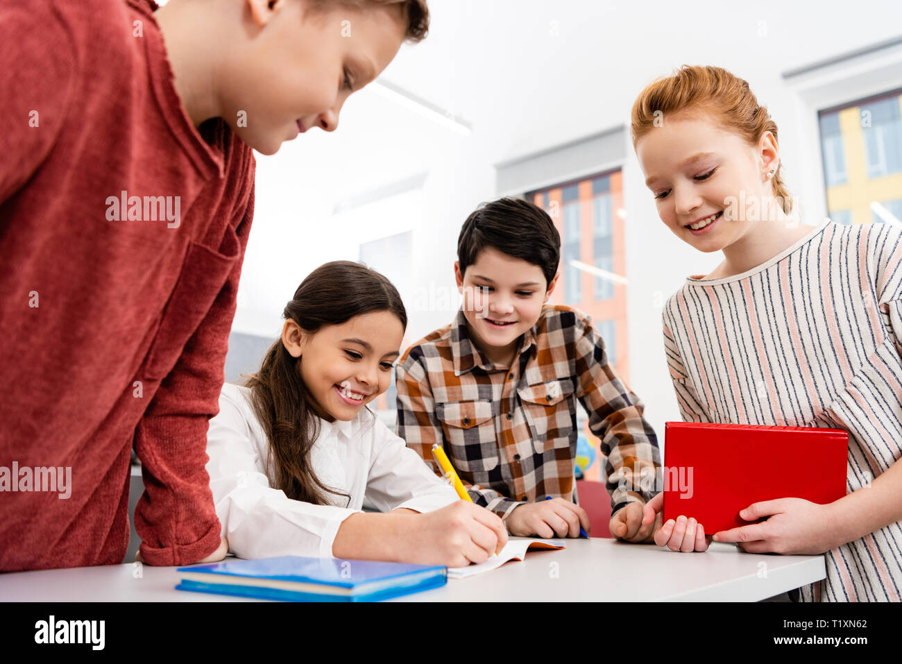 Smiling pupils with notebook and books discussing in classroom Stock ...