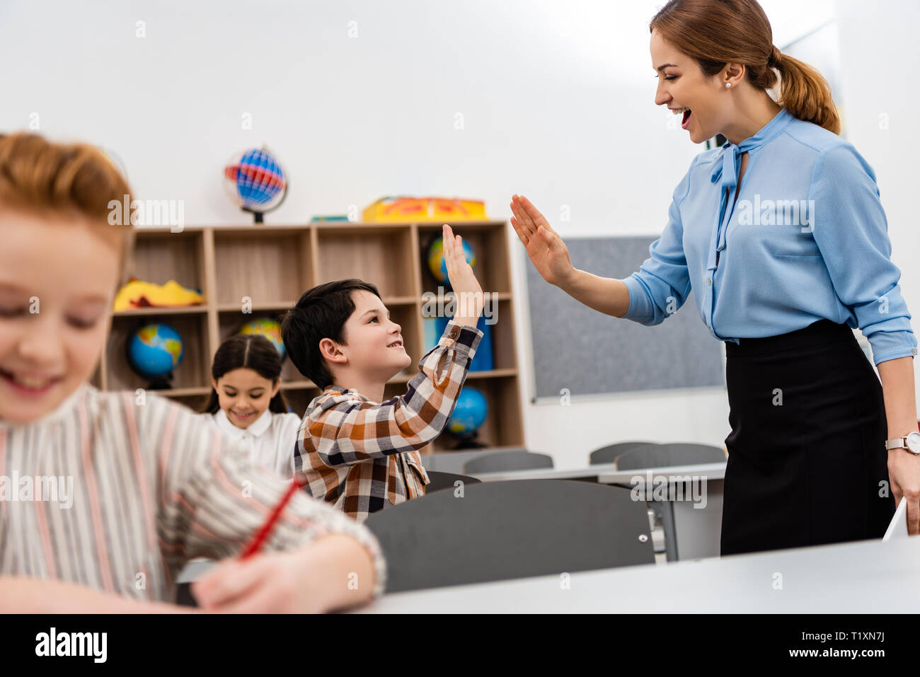 Smiling teacher and pupil raising hands for high five in classroom ...