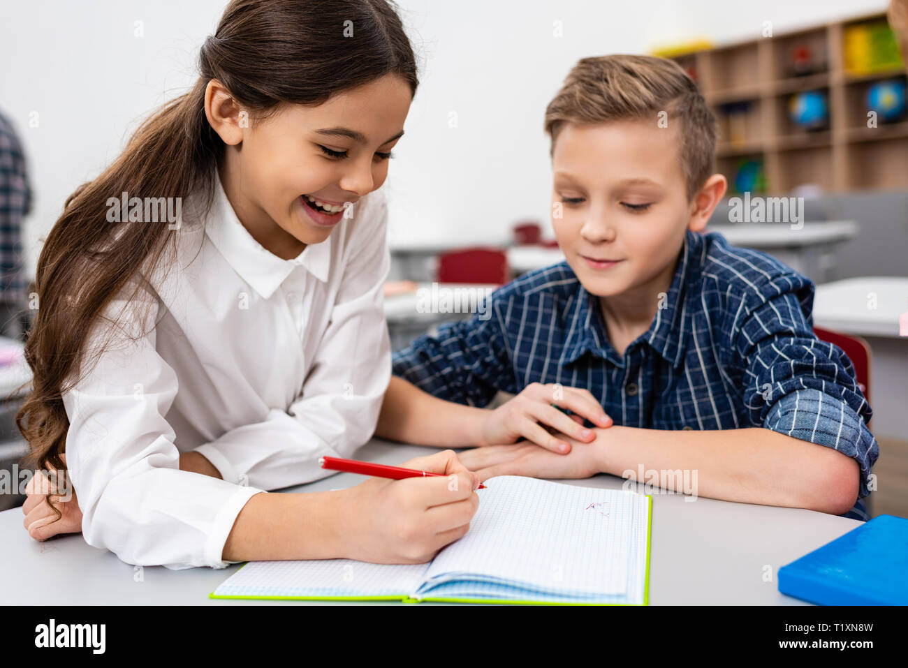 Two pupils writing in notebook at desk in classroom Stock Photo - Alamy