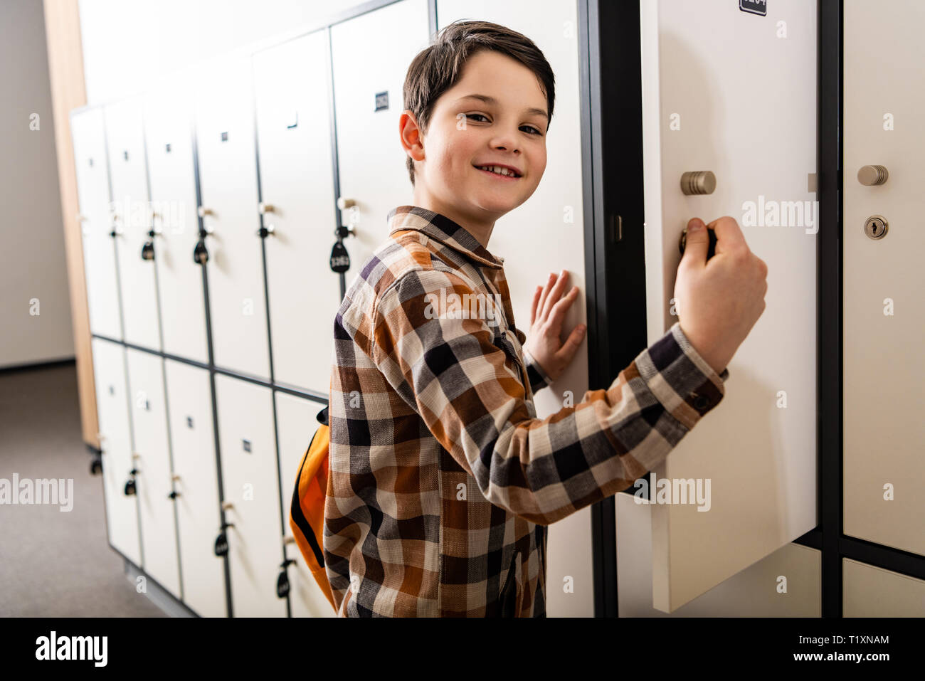 Smiling schoolboy in checkered shirt with backpack opening locker Stock ...
