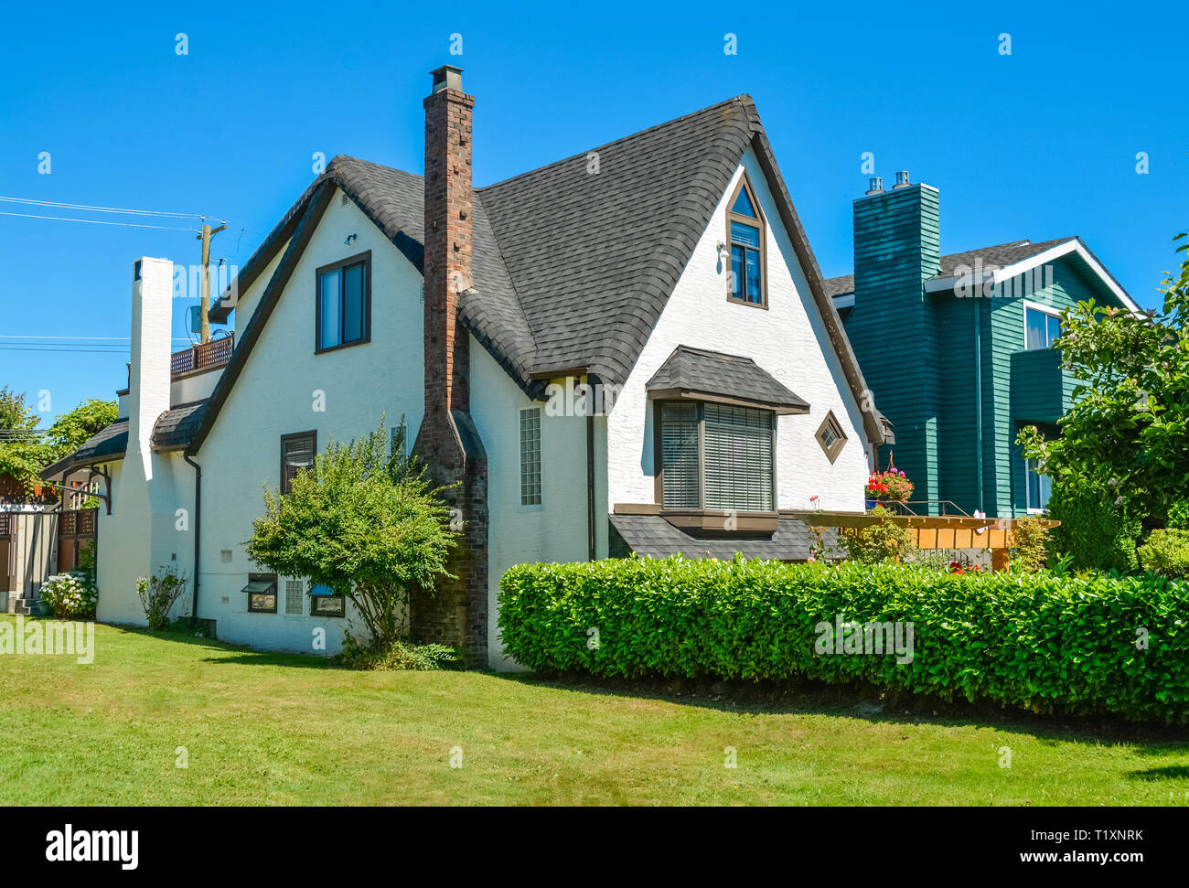 Old style family house with lawn and hedgerow in front on blue sky ...