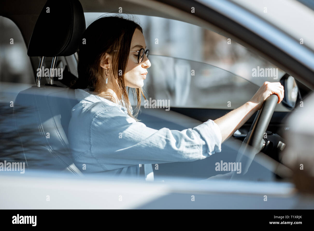 Young and happy woman driving luxury car in the city, side view through ...