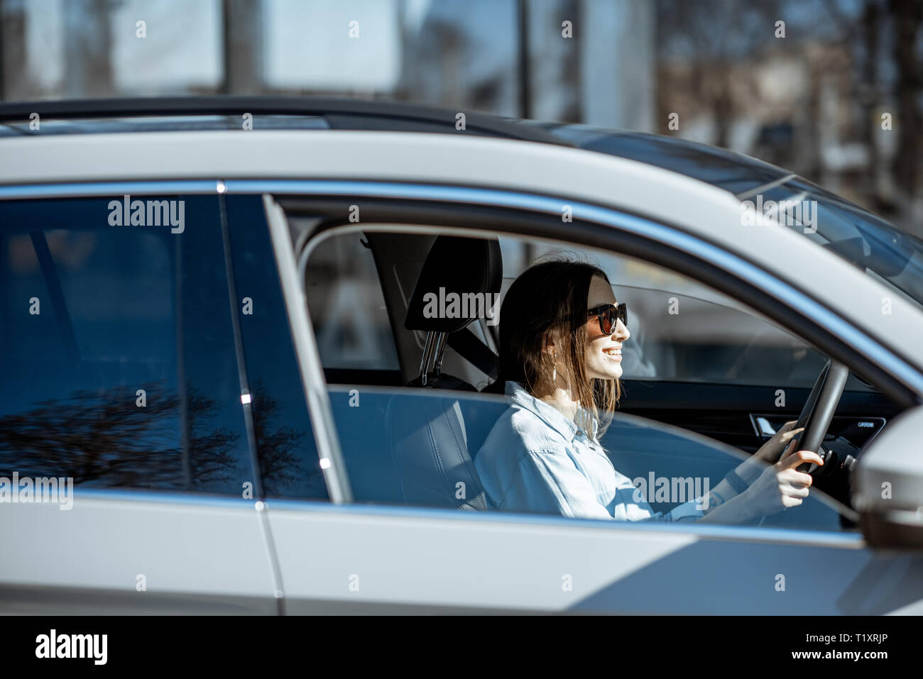 Young and happy woman driving luxury car in the city, side view through ...