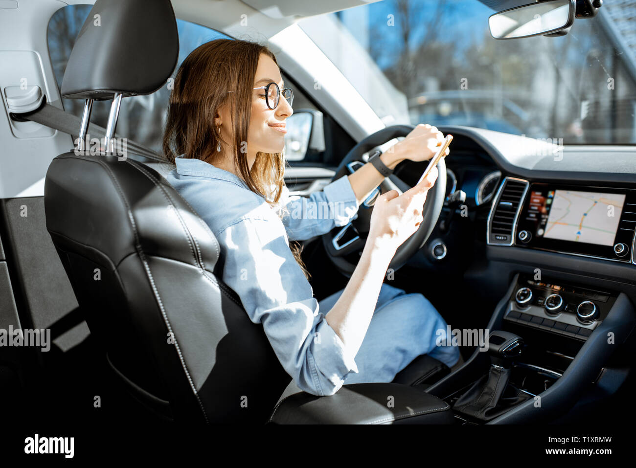 Young and cheerful woman using smart phone while driving a modern car ...