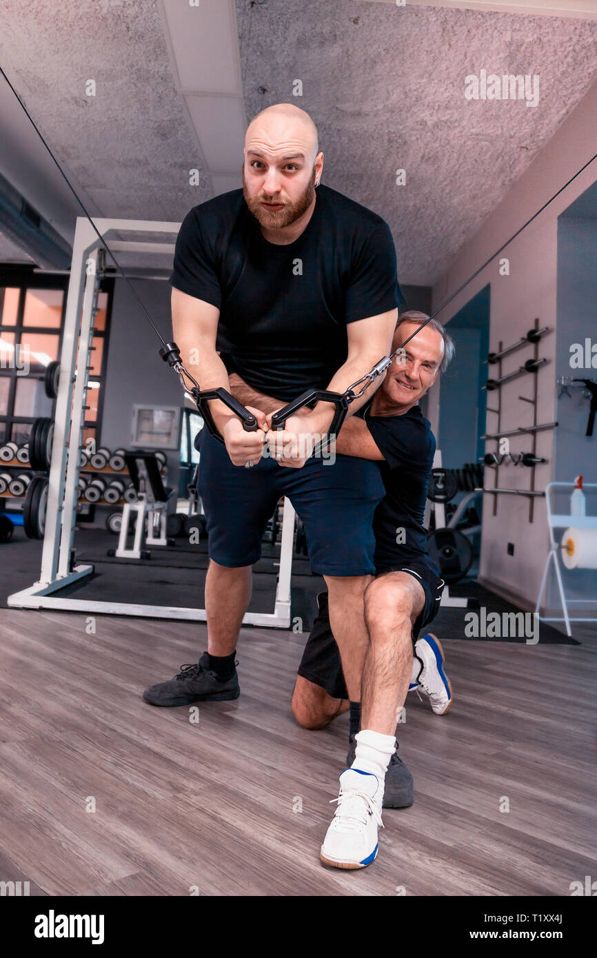 two friends athletes have fun while exercising at the cables in the gym ...