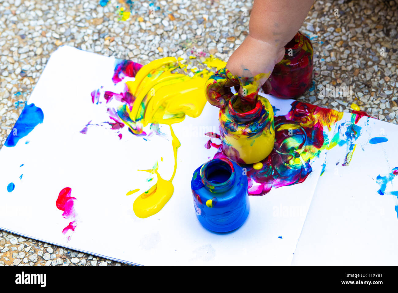 child hand draws a finger paint - blue, red and yellow on a white sheet ...