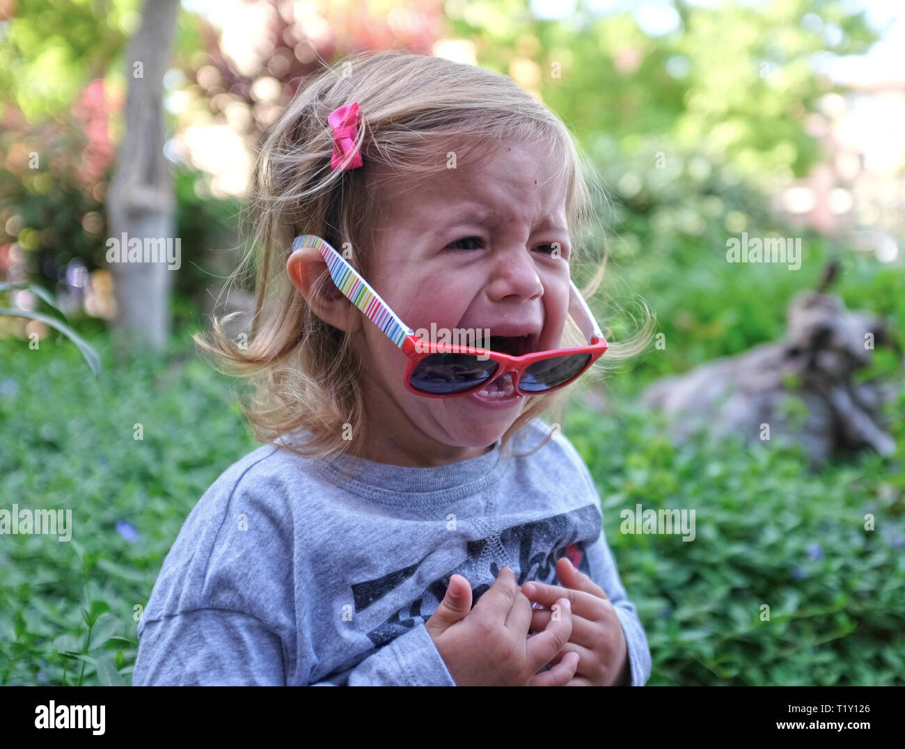 Little girl crying in the garden on spring background. Sad and angry ...
