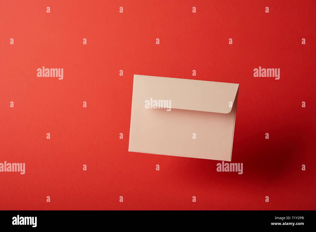 beige, blank and empty envelope on bright red background with copy ...