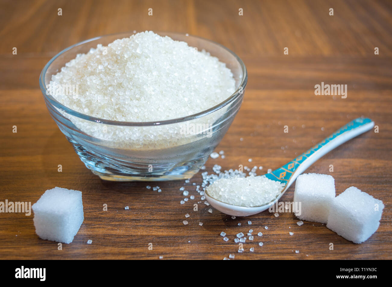 White sugar kept in a glass bowl with a spoon. Some sugar cubes kept on ...