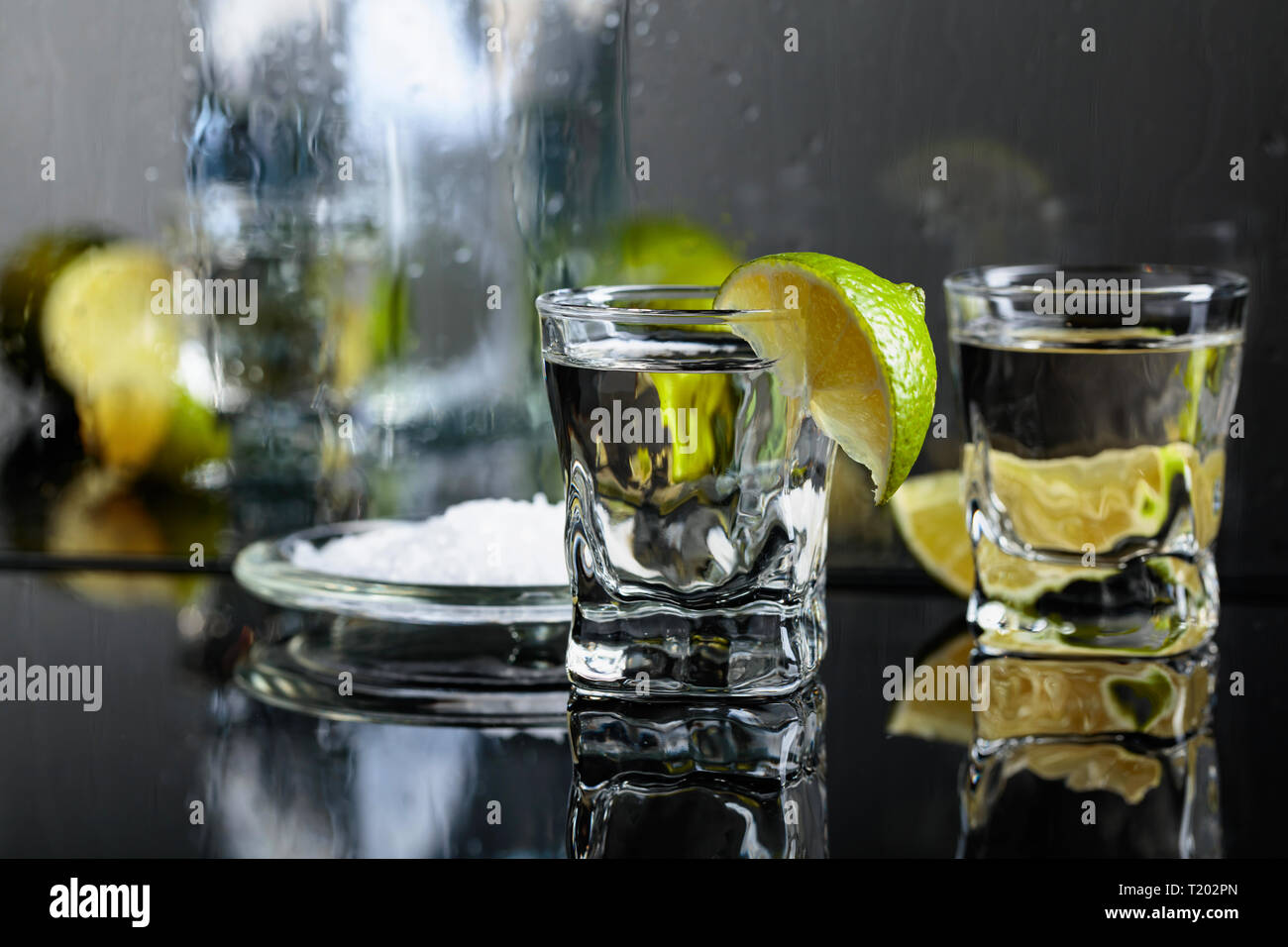 Glasses of tequila with lime and salt on the black reflective ...