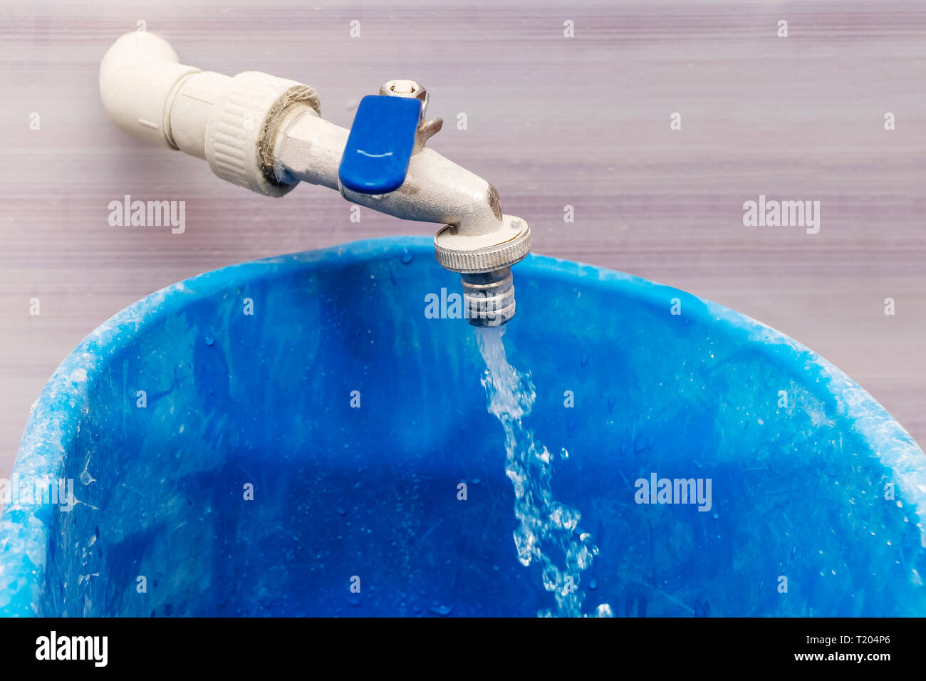 from the open dirty tap flows a stream of water in a blue bucket Stock ...