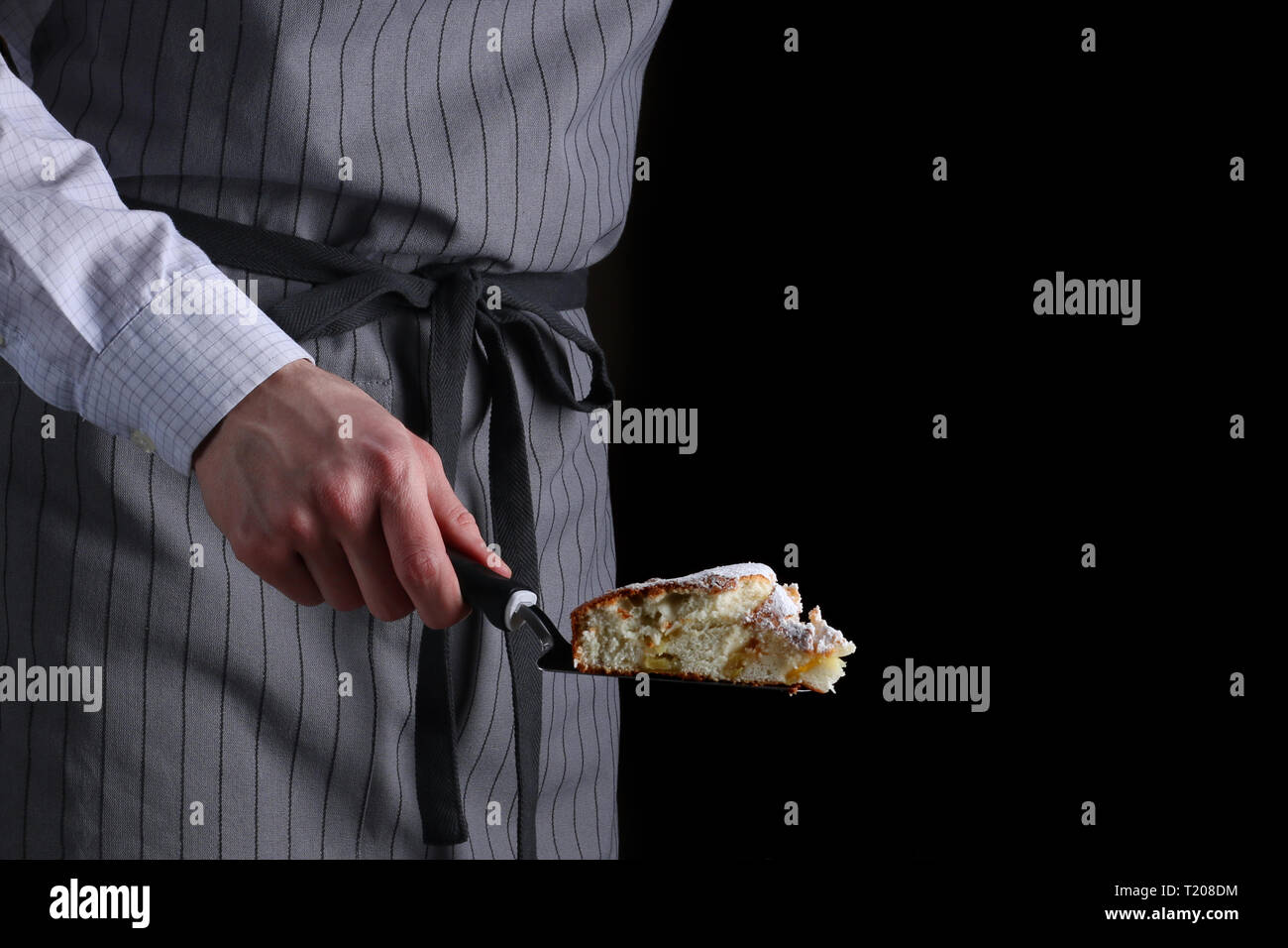 chef holding a piece of cake on black background. pie making and serve ...