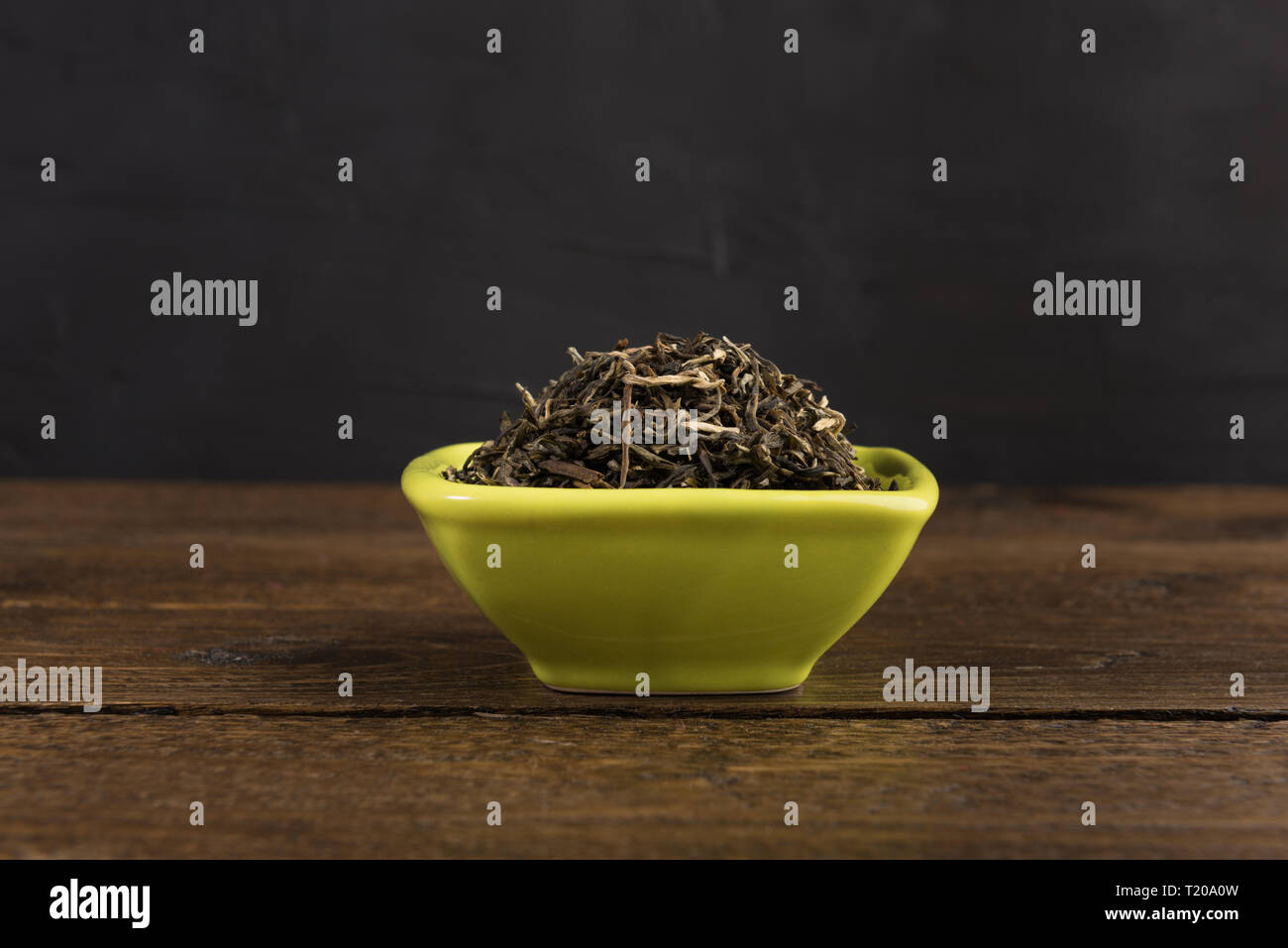 dry green tea in a clay bowl isolated on wooden table on black ...