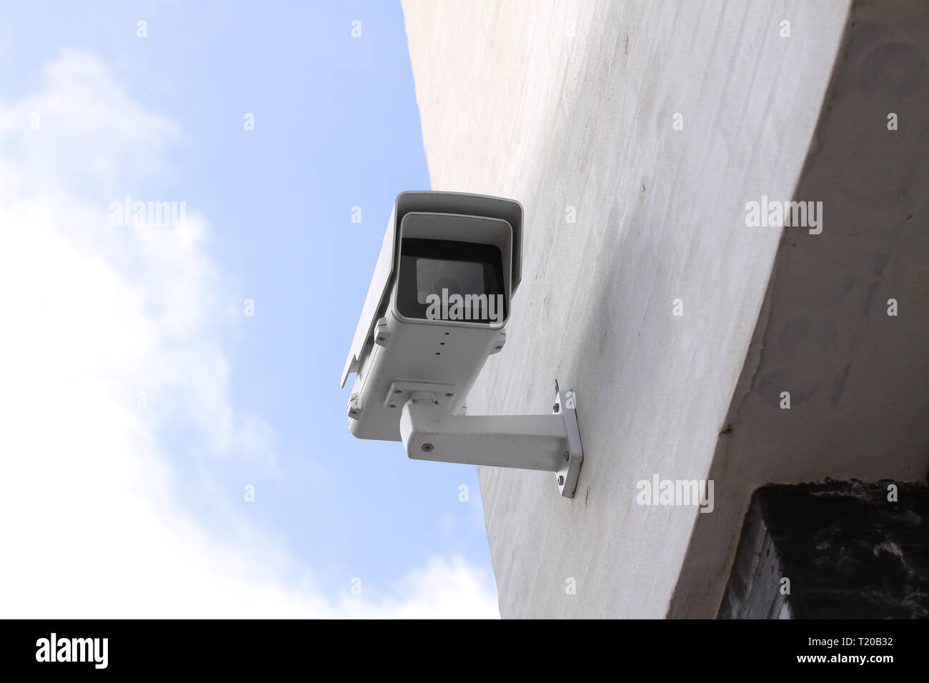CCTV survaillance camera mounted on white building with blue sky in ...