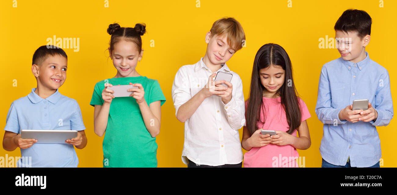 Gadget addiction. Children with modern gadgets standing over yellow ...