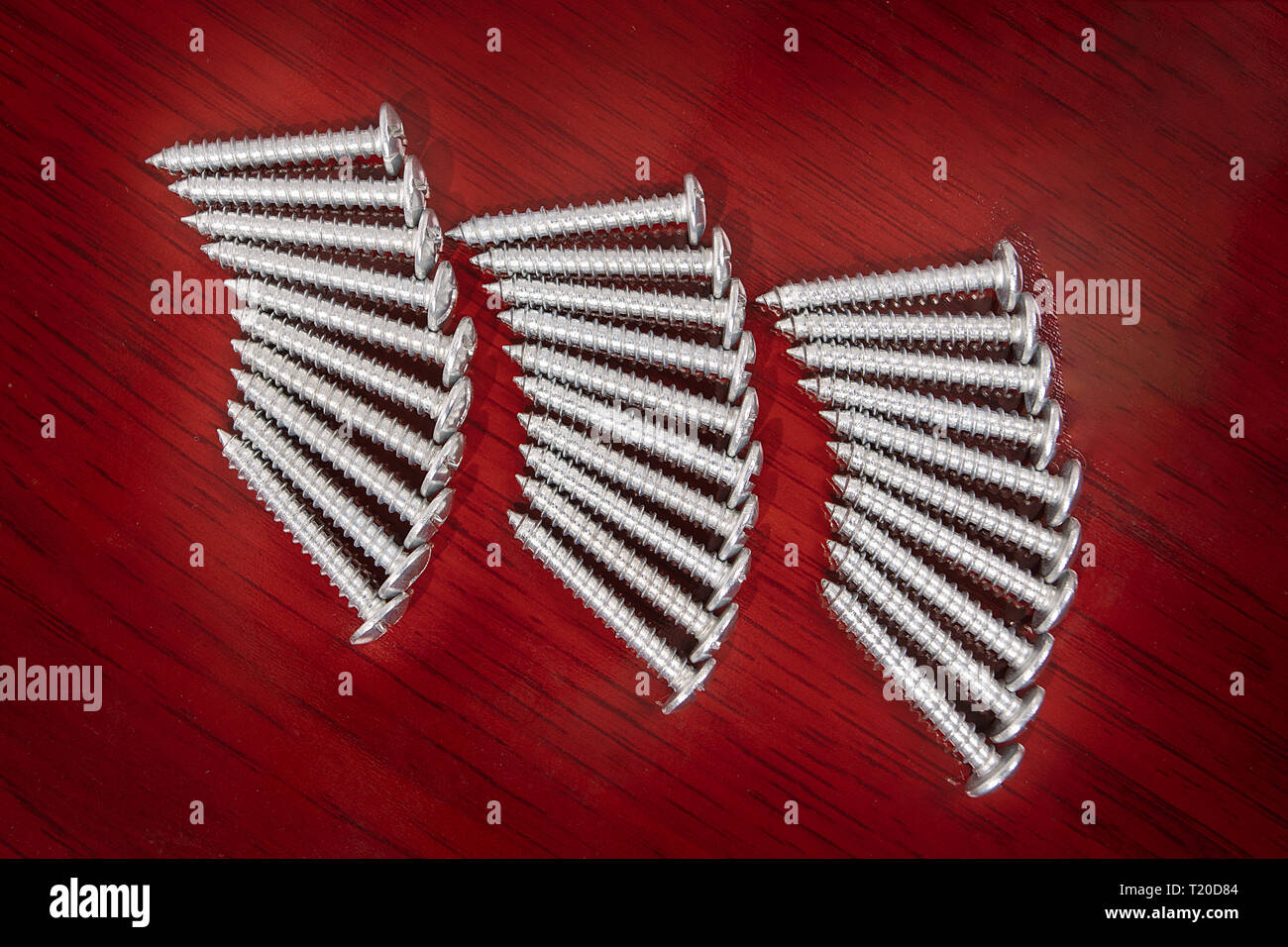 Three groups of silver screws arranged in rows on a surface with wooden ...
