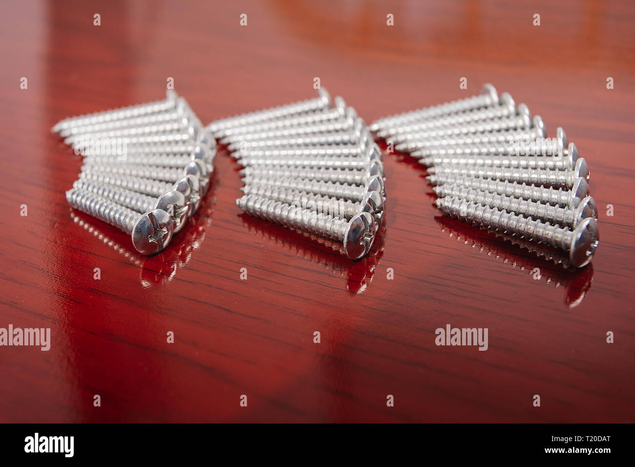 Three groups of silver screws arranged in rows on a surface with wooden ...