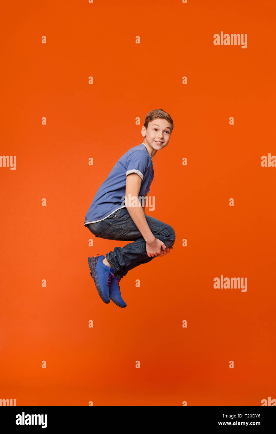 Emotional boy jumping in bomb style, orange studio background Stock ...
