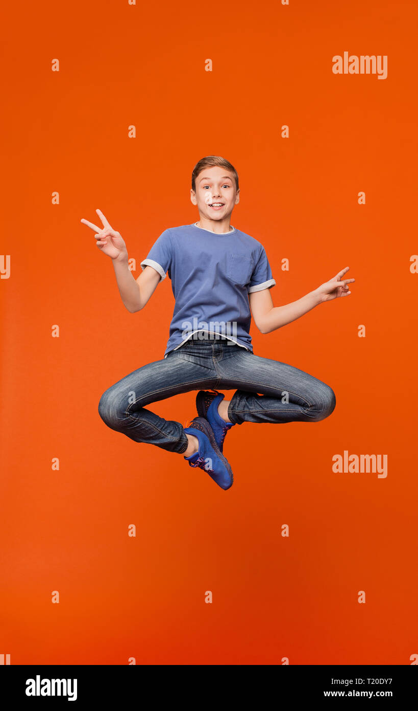 Cute boy jumping and gesturing peace signs on orange studio background ...