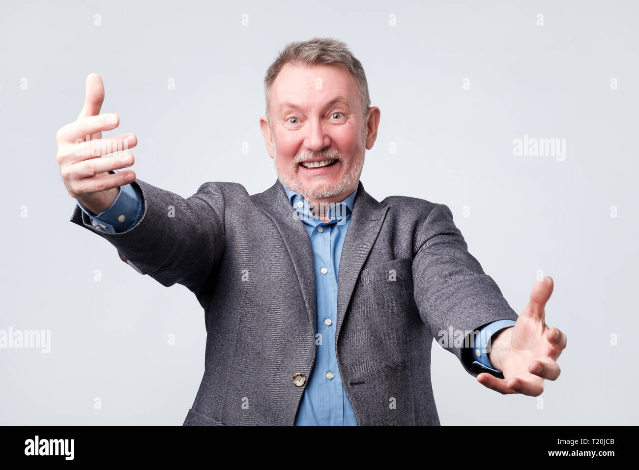 Senior man in suit joyfully stretches hands forward on a white ...