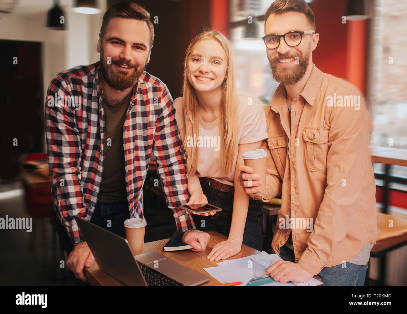 Happy guys and girl are standing near table with business materials and ...