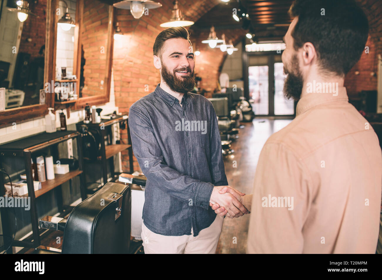 Guy in blue shirt is shaking the hand of the customer of barber shop ...