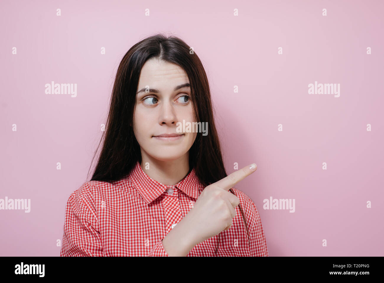 Beautiful puzzled young woman clenches smile, shows direction aside ...