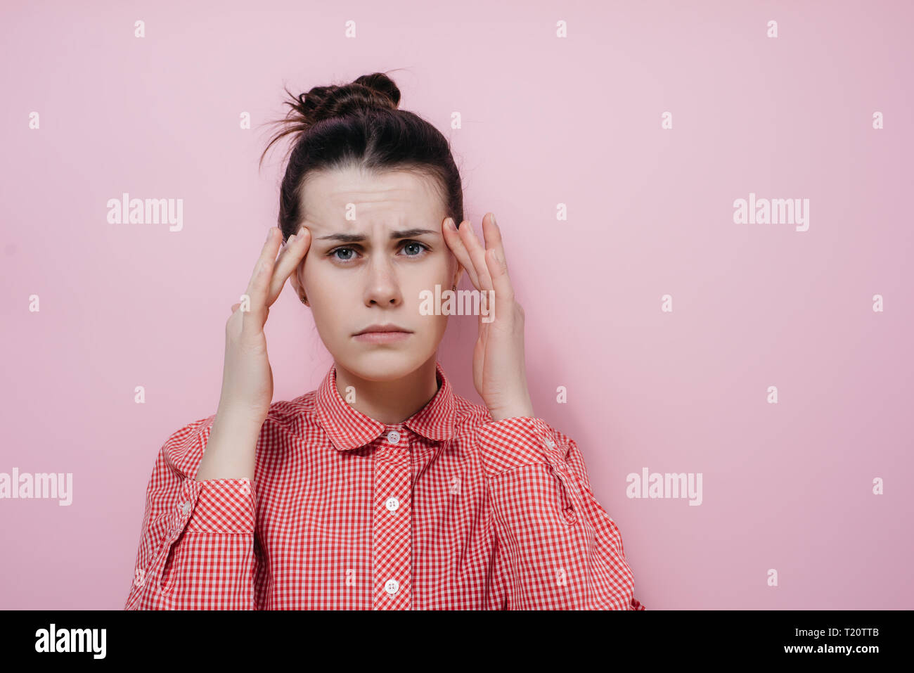Young tired brunette woman wears red shirt, keeps finger on temples ...