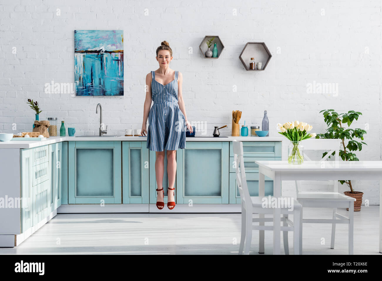 smiling pretty girl levitating in air in turquoise and white kitchen ...