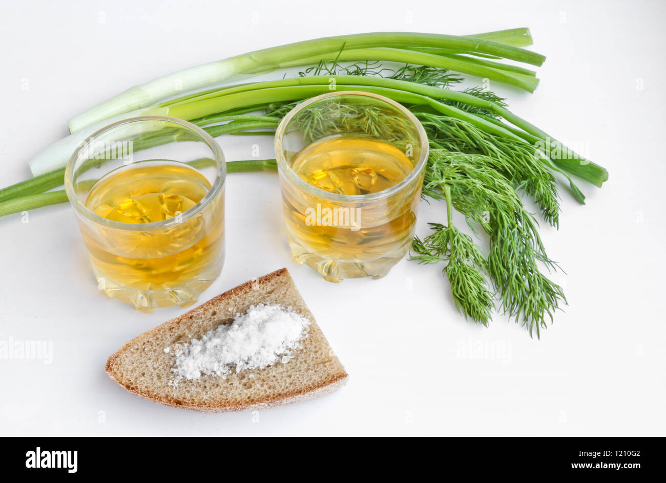 Pepper vodka in two transparent glasses, green onions, dill, rye bread ...