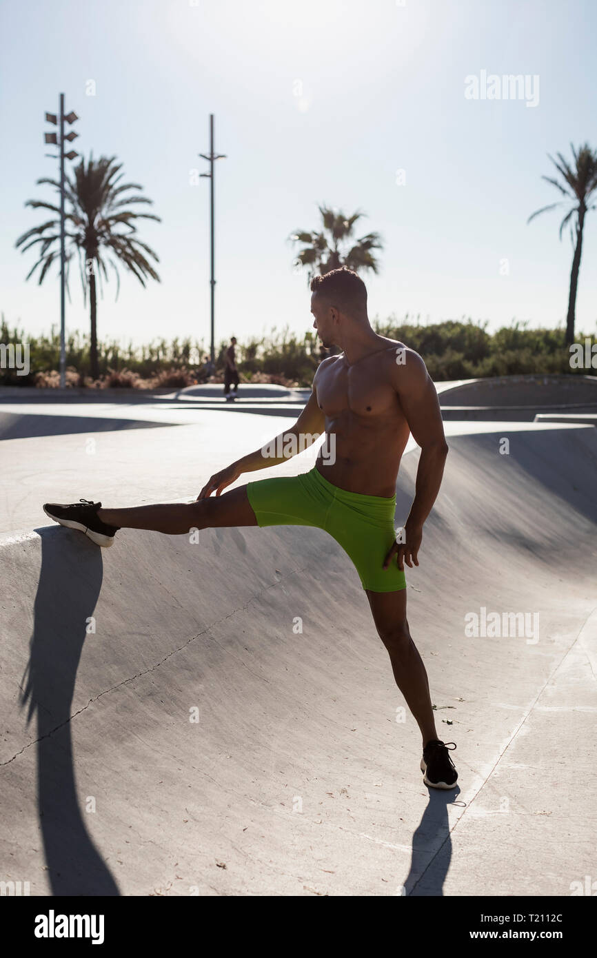 Barechested muscular man doing stretching exercise in a skatepark Stock ...