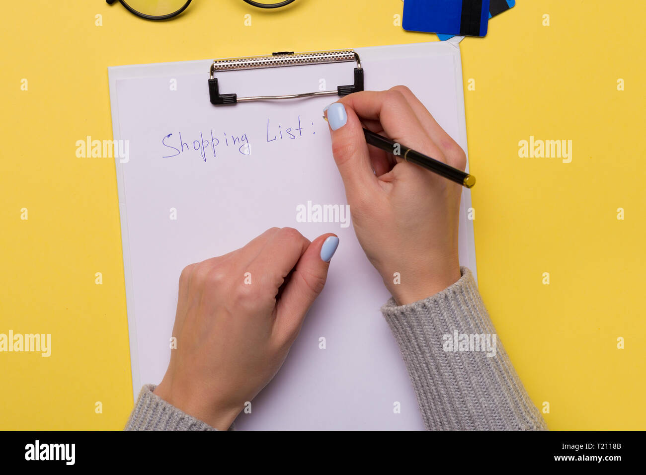 Woman hands writing a shopping list on a yellow background. Free space ...