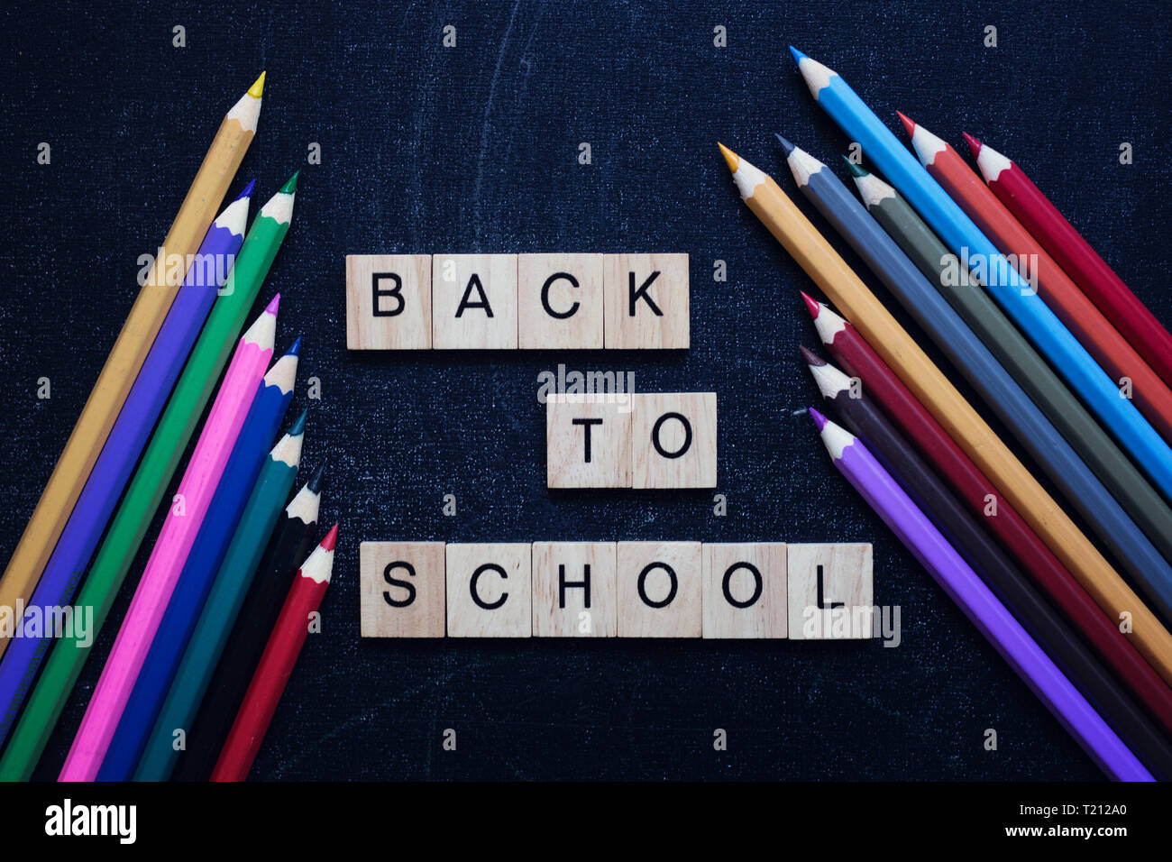 Coloured pencils around wooden words back to school on slate black ...