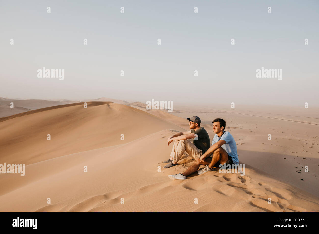 Namibia, Namib, two friends sitting on desert dune looking at view ...