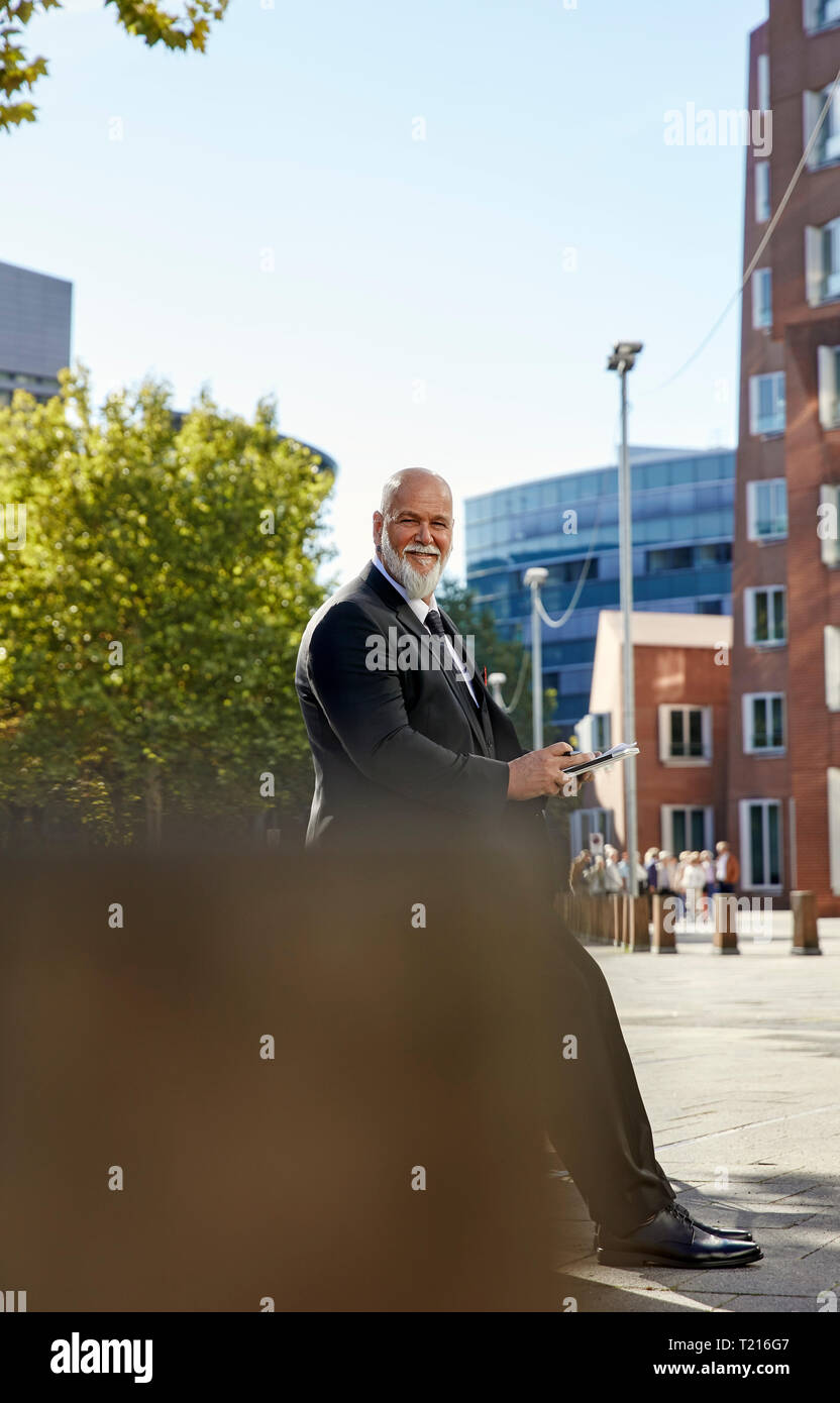 Elegant businessman leaning on wall in the city, using digital tablet ...