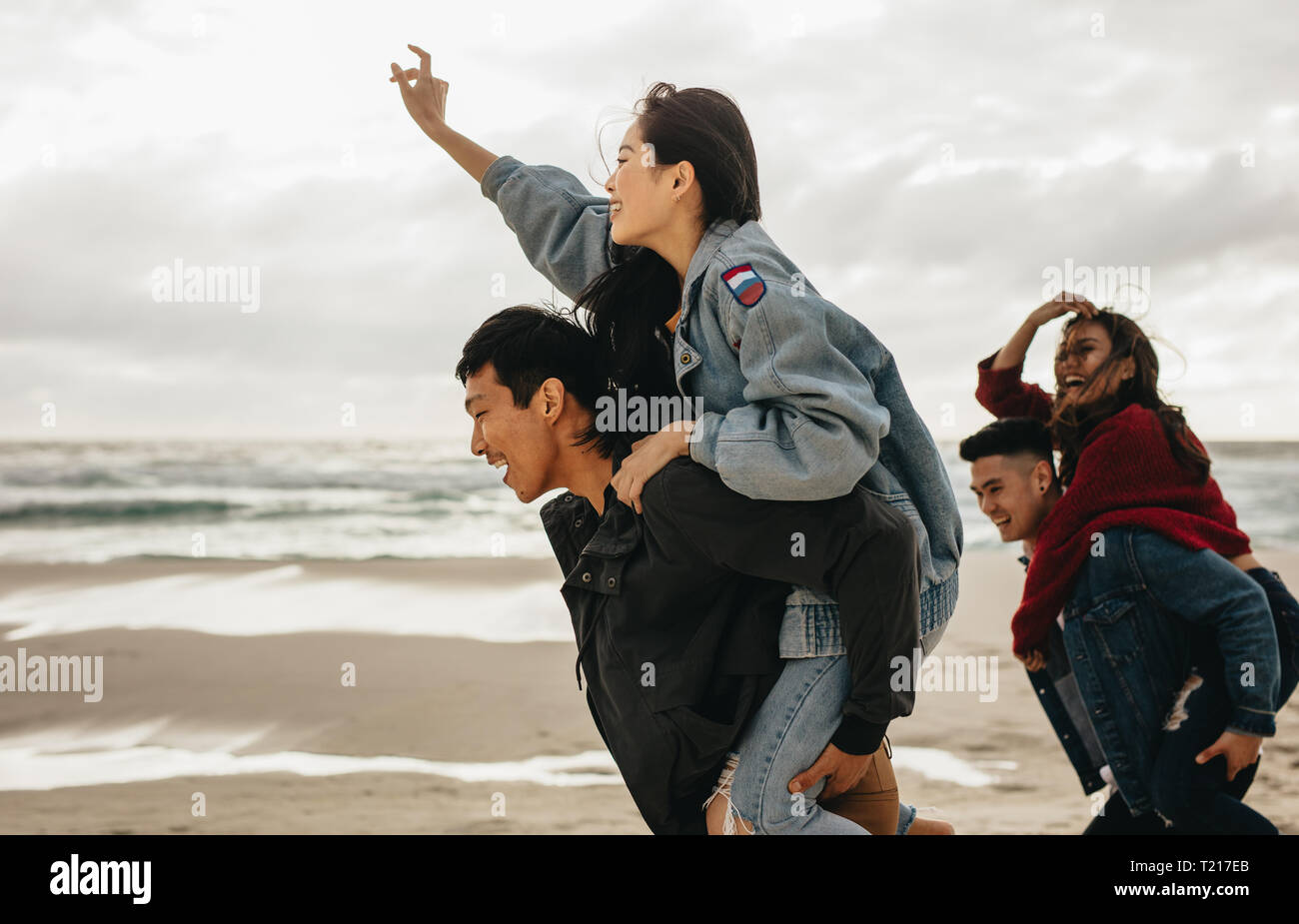 Two young men giving their girlfriends piggyback rides at the beach ...