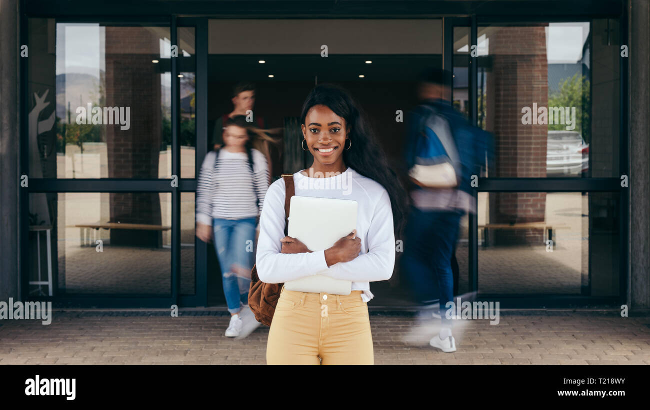 Portrait of girl student standing at university campus with other ...