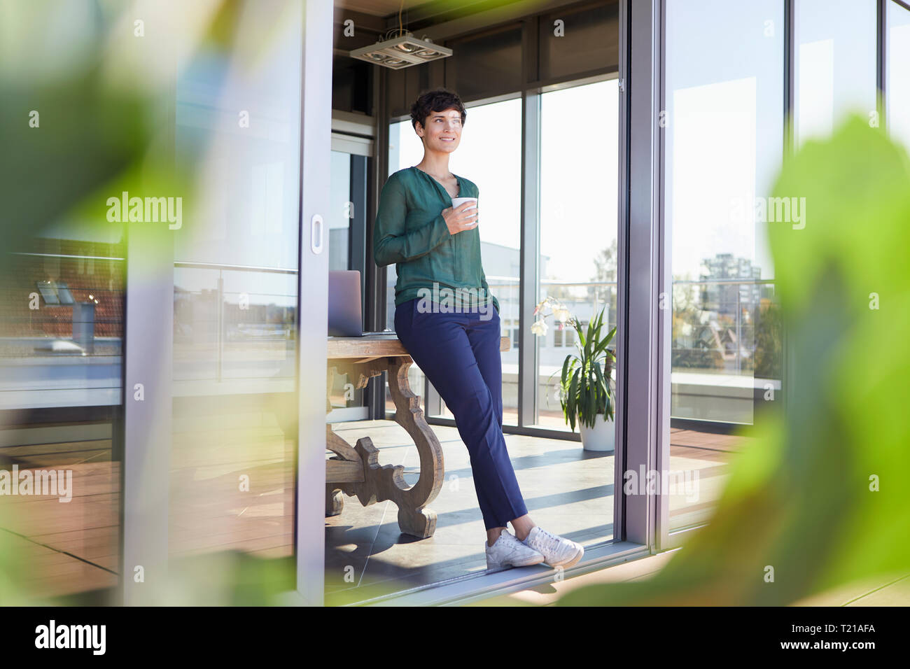 Smiling businesswoman leaning against table having a coffee break Stock ...