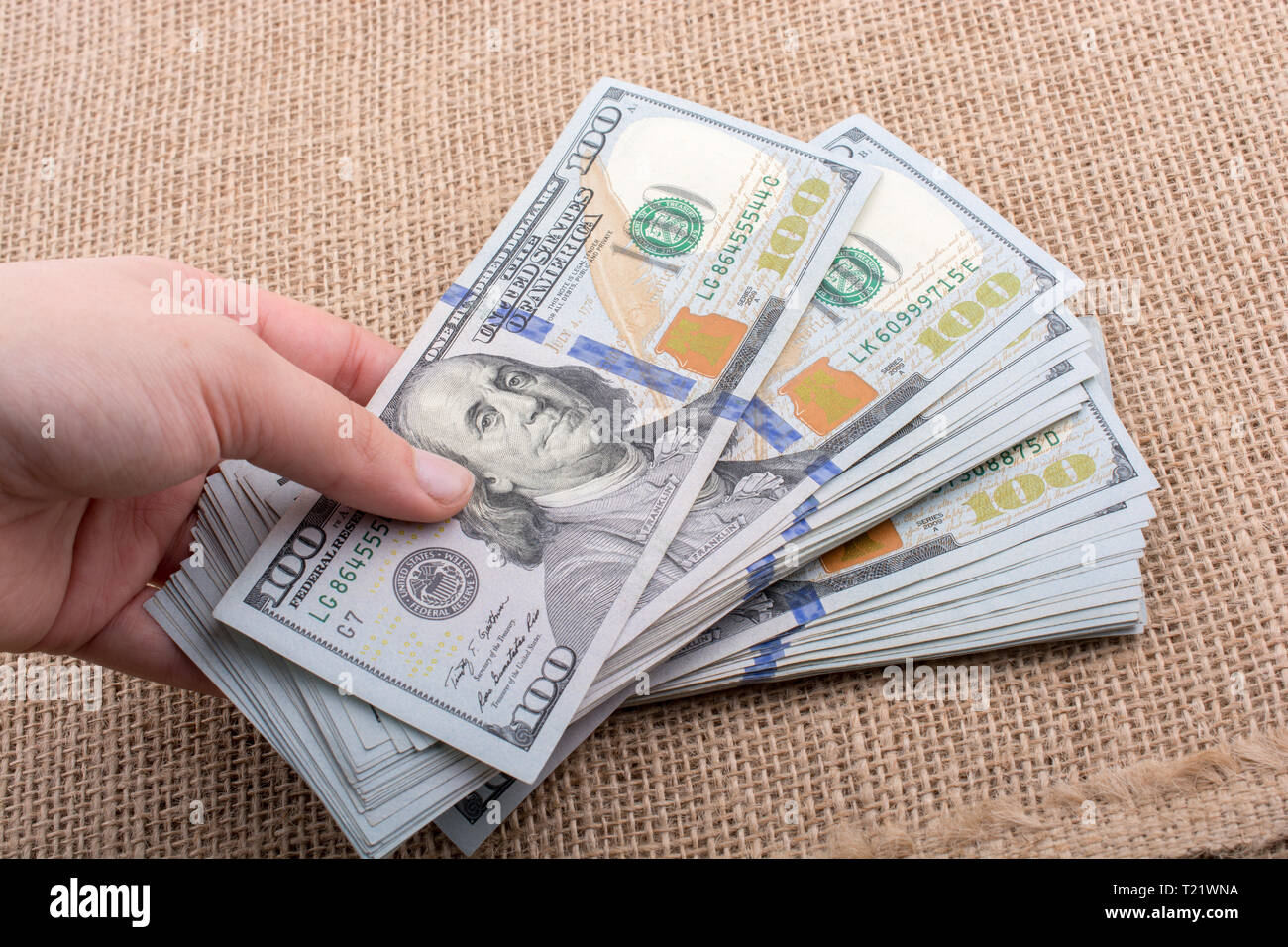 Hand holding banknote bundle of US dollar on a linen canvas background ...