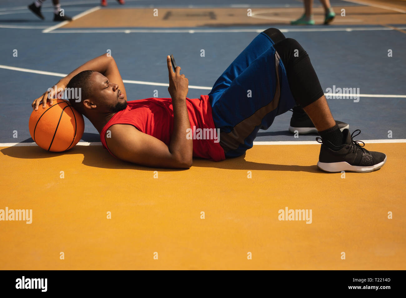 Basketball player using mobile phone while relaxing on basketball court ...