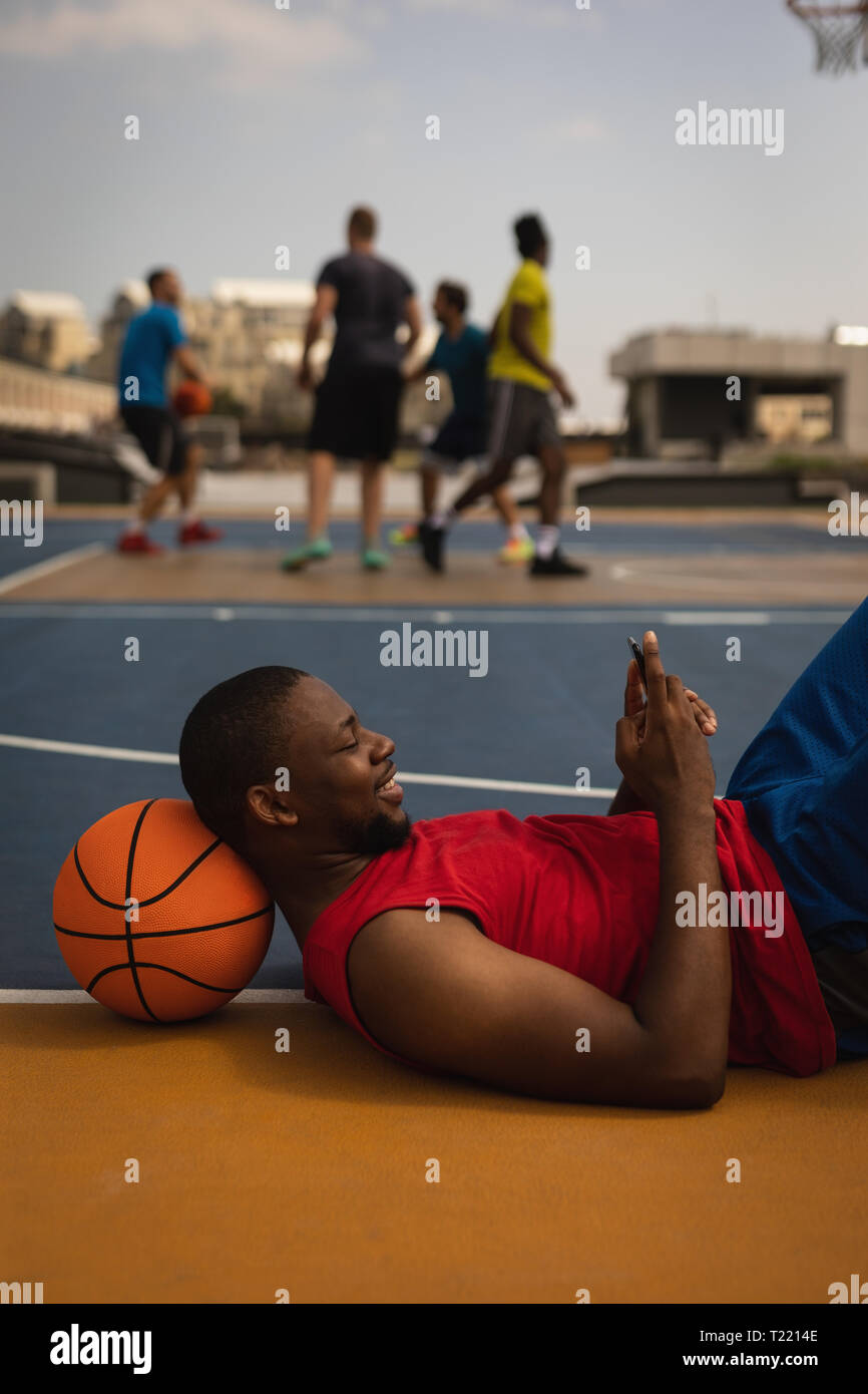 Basketball player using mobile phone while relaxing on basketball court ...