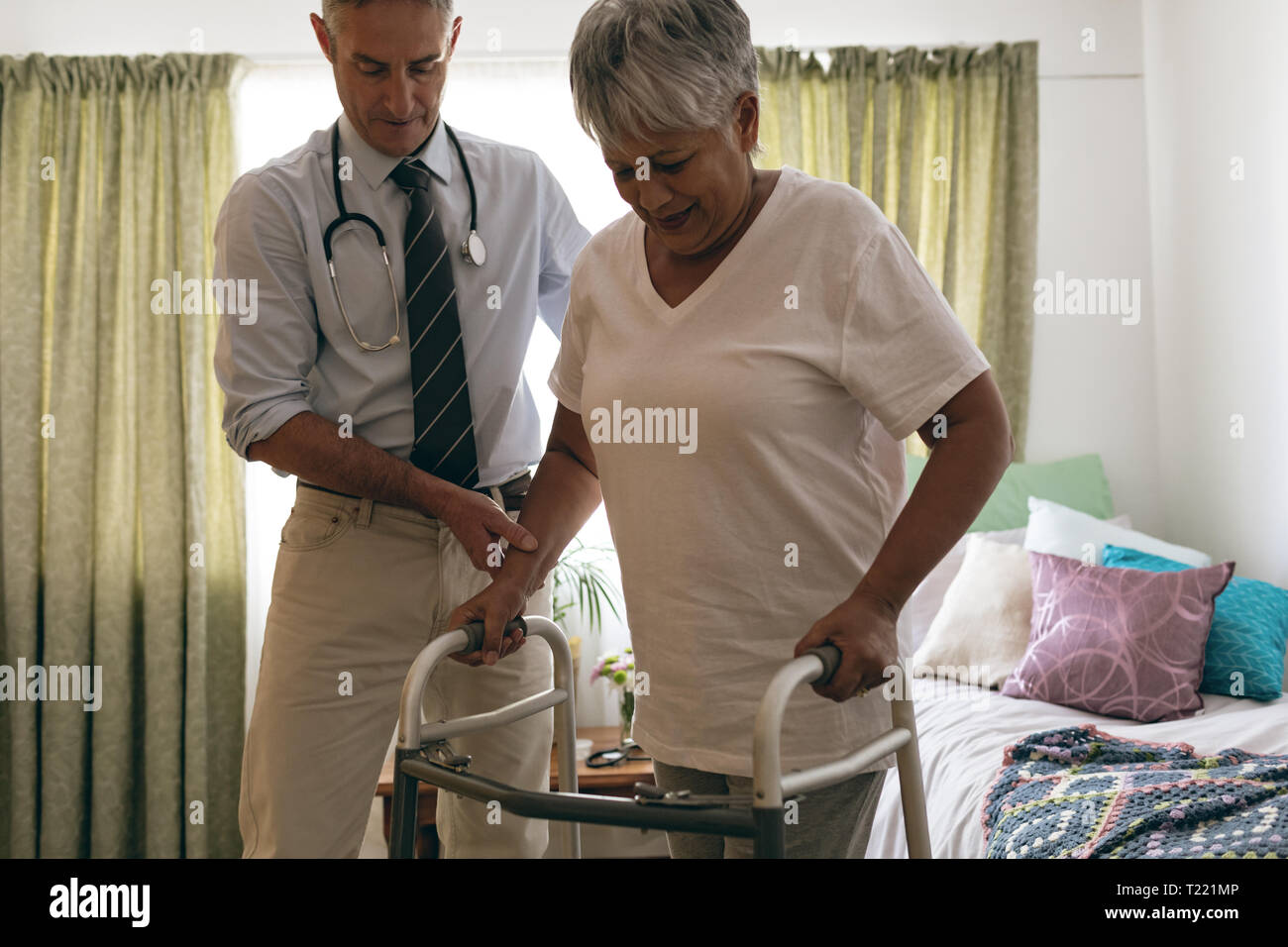 Male doctor helping senior female patient to walk with walker Stock ...