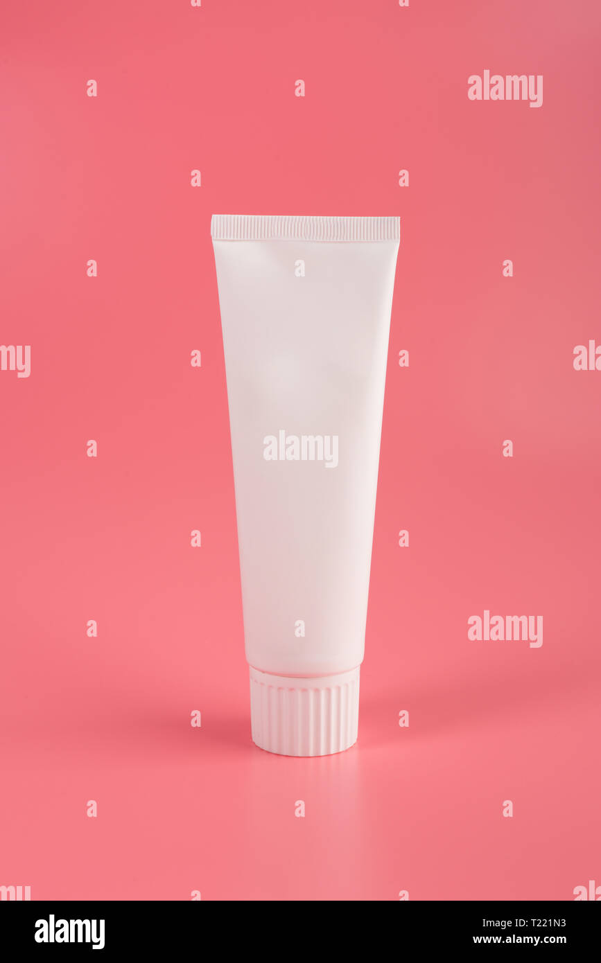 Blank white tube of toothpaste, cream or gel standing on pink ...