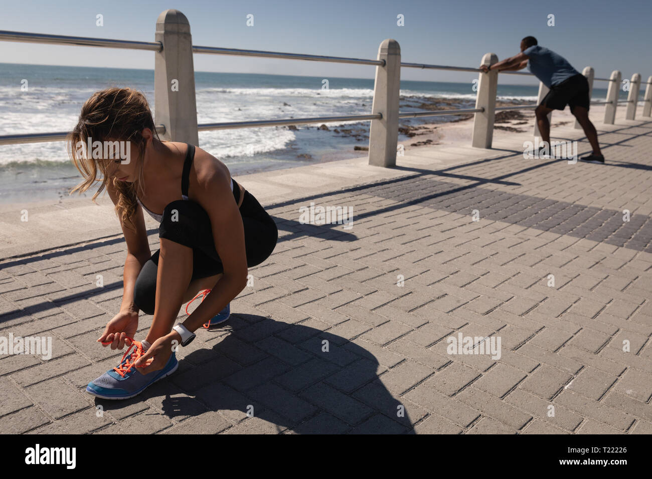 Beautiful woman tying shoe lace while man doing stretching exercise ...
