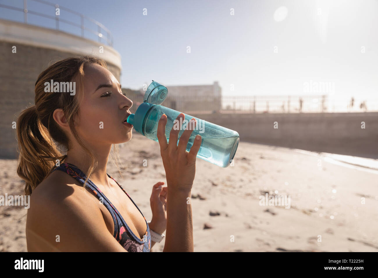 Beautiful woman drinking water with bottle while standing at beach ...