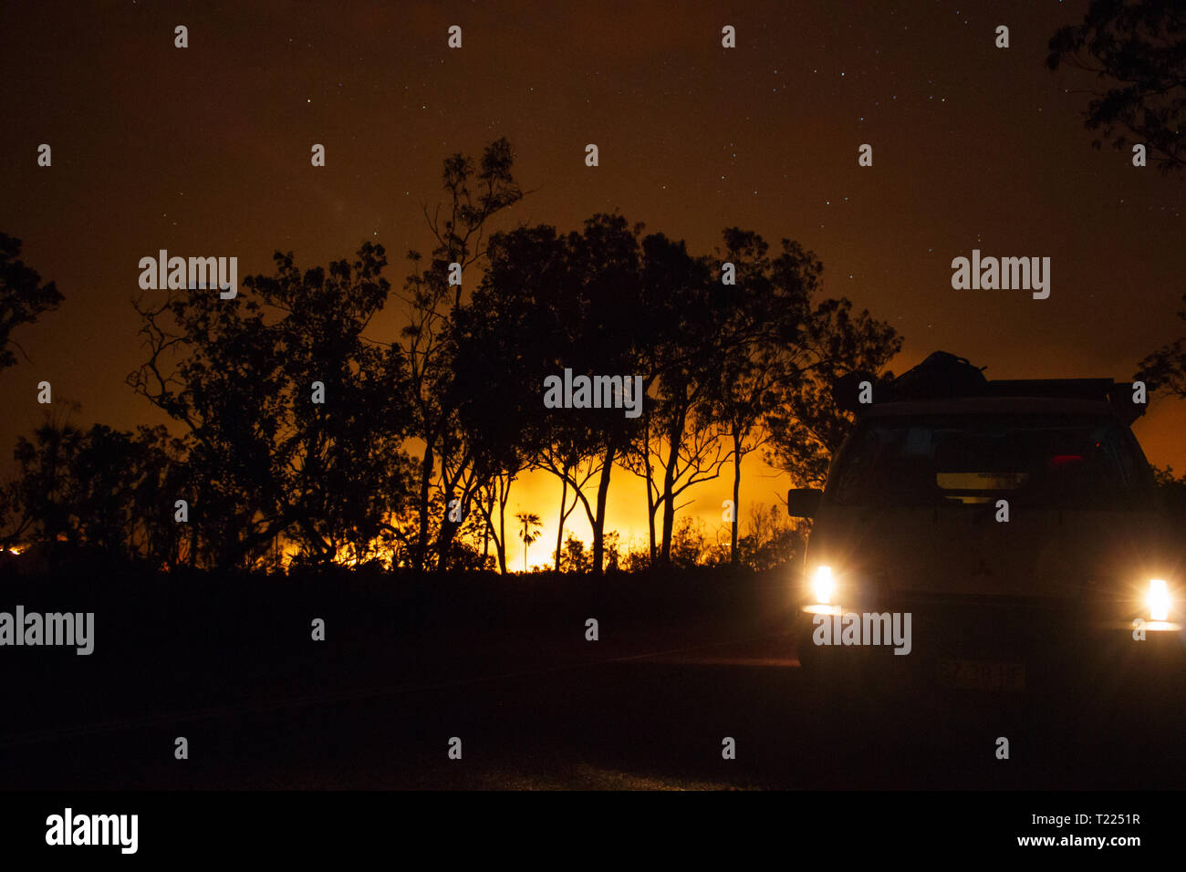 car driving away from a bushfire, forest are really bright because of ...