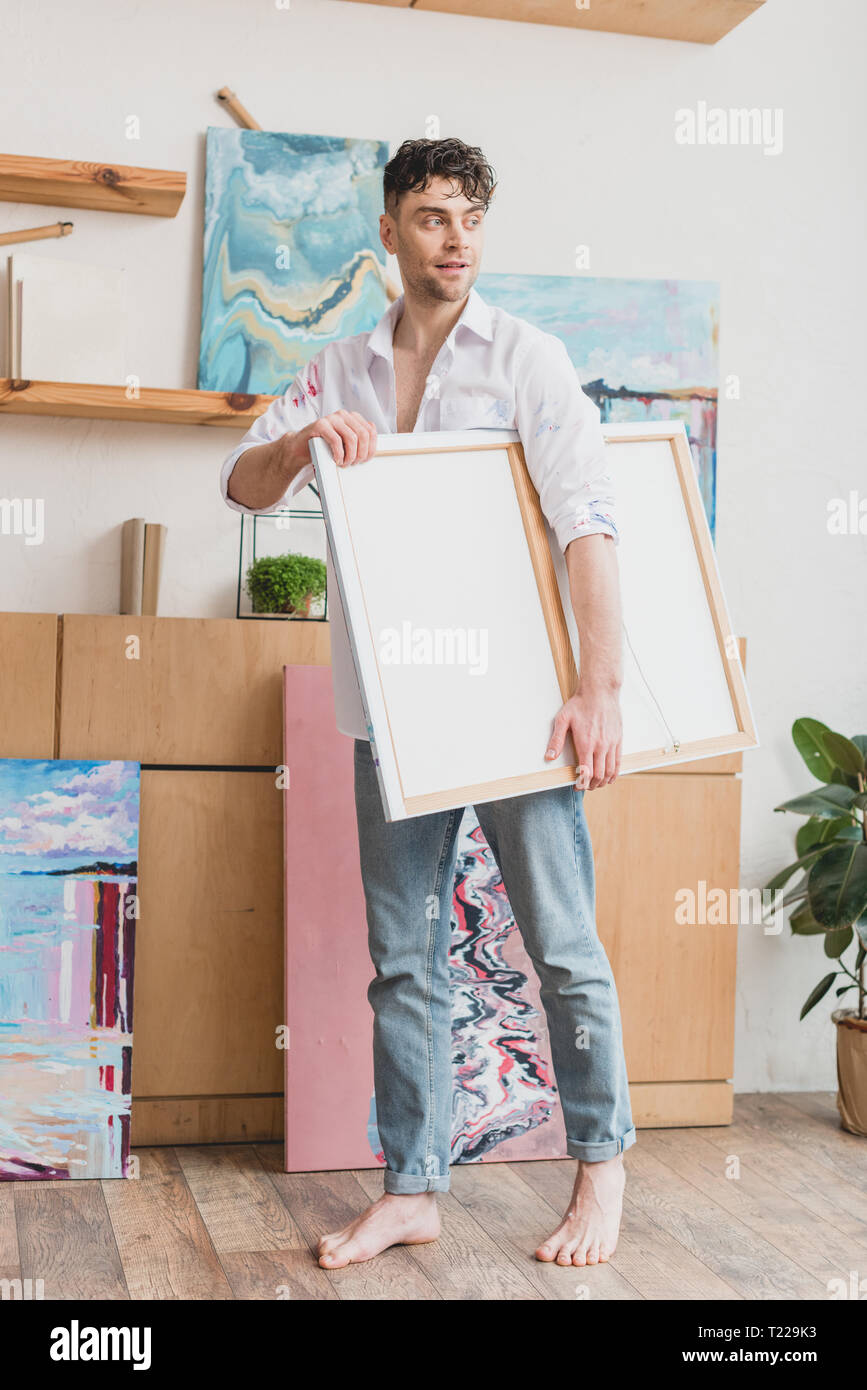 good-looking artist in white shirt and blue jeans carrying canvas in ...