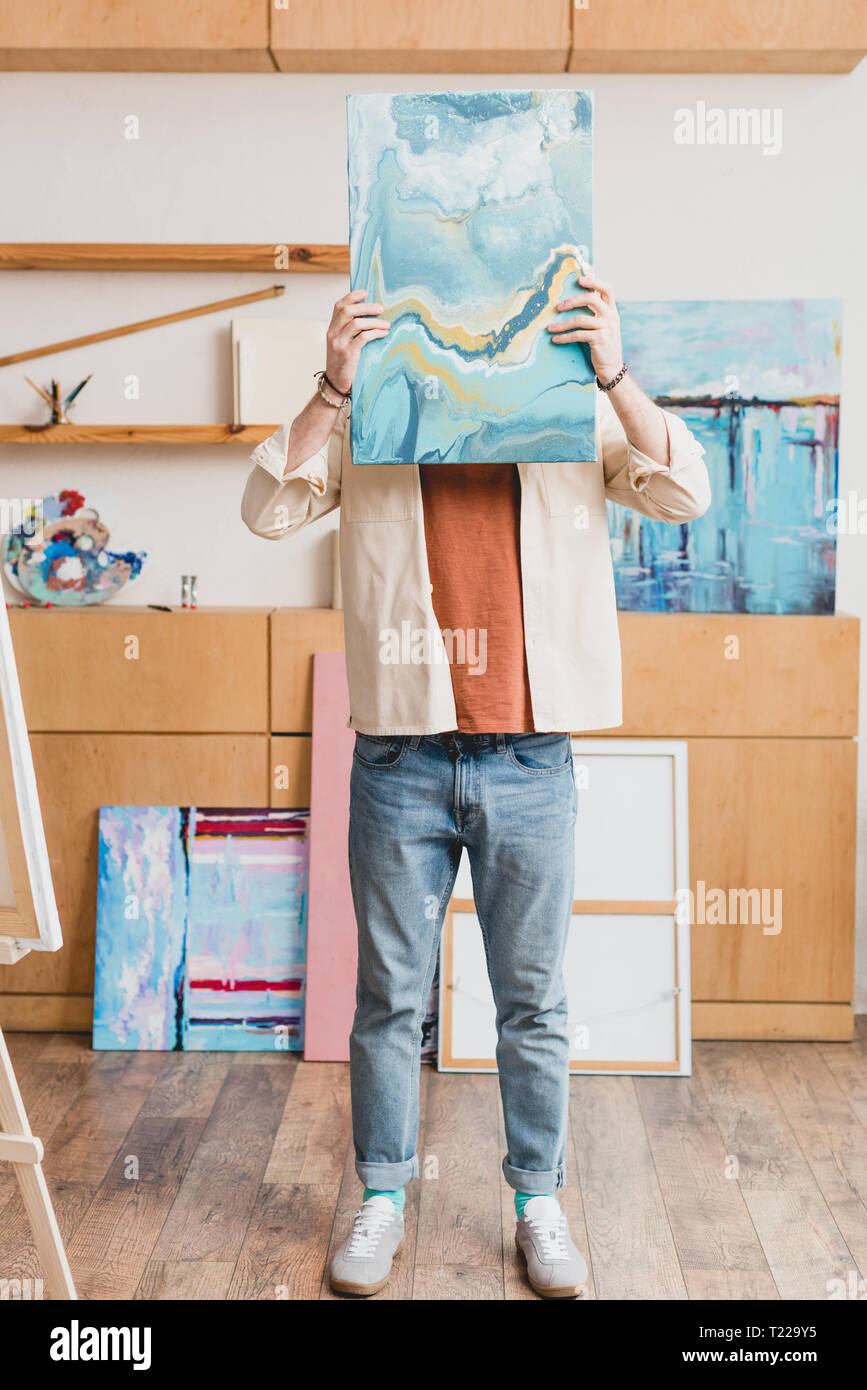 artist standing in painting studio and hiding face behind colorful ...