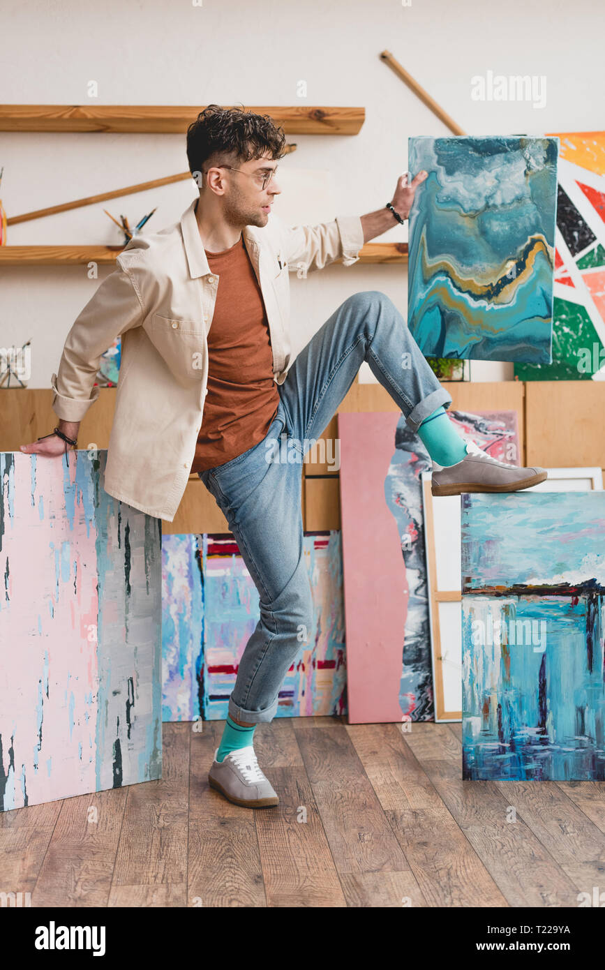good-looking artist holding multicolored abstract paintings in painting ...